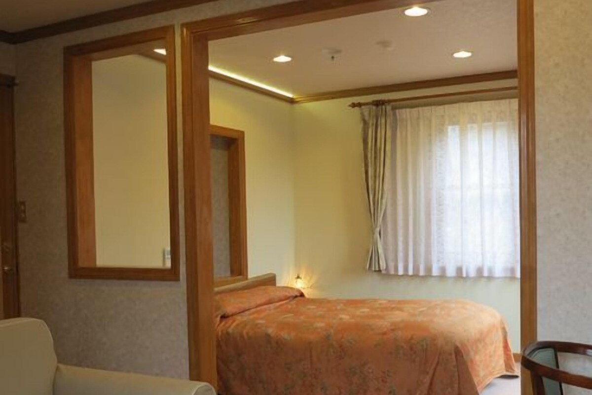Quarto com cama, poltrona, sofá e mesa pequena.