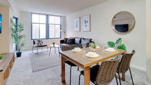 Uma sala de estar moderna com área de jantar, apresentando um sofá, mesa de centro e mesa de jantar posta com pratos e copos.