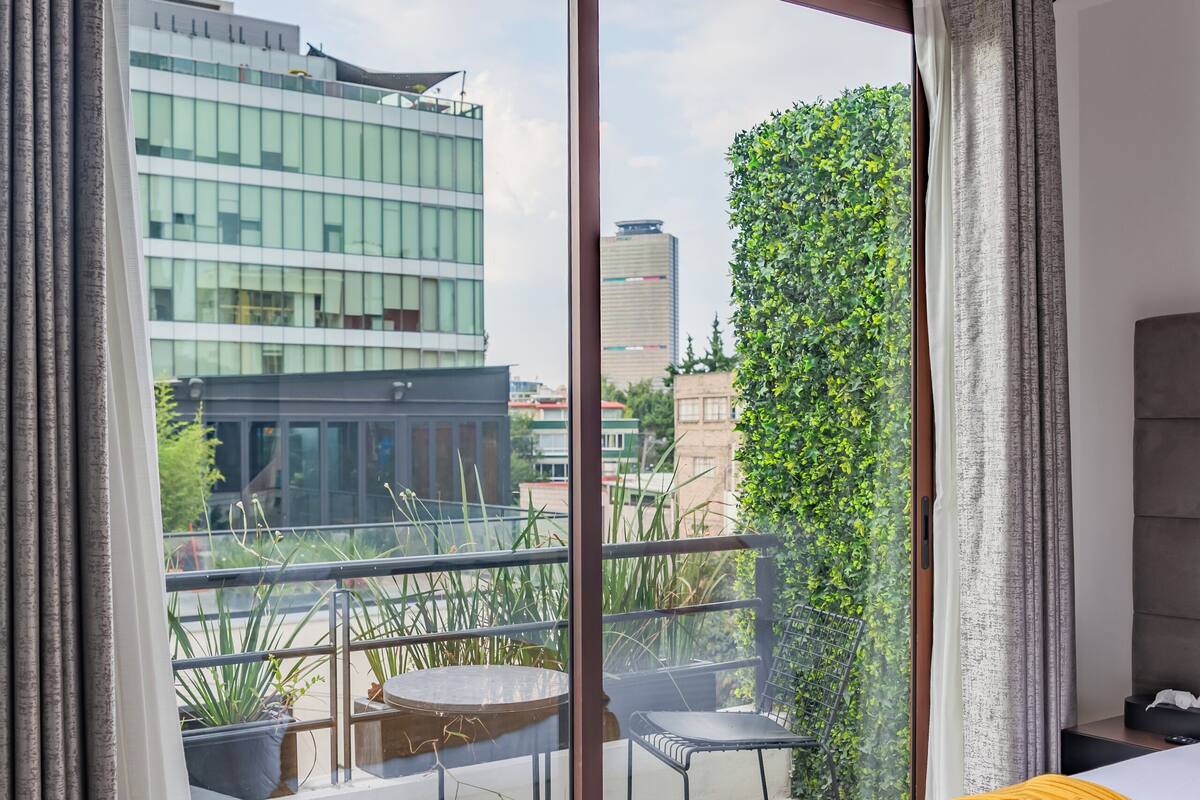 Quarto com uma grande porta de vidro deslizante que dá para uma varanda com vista para um edifício moderno e vegetação.