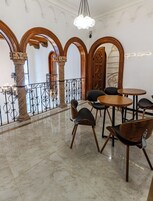 Interior espaçoso com piso de mármore, cadeiras e mesas de madeira, detalhes em arcos ornamentados e um lustre.