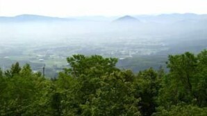 Vista de um vale com montanhas ao fundo e vegetação verde densa em primeiro plano.