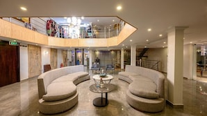 Um hall amplo com área de estar em curva, uma mesa central e um mezanino com lojas.