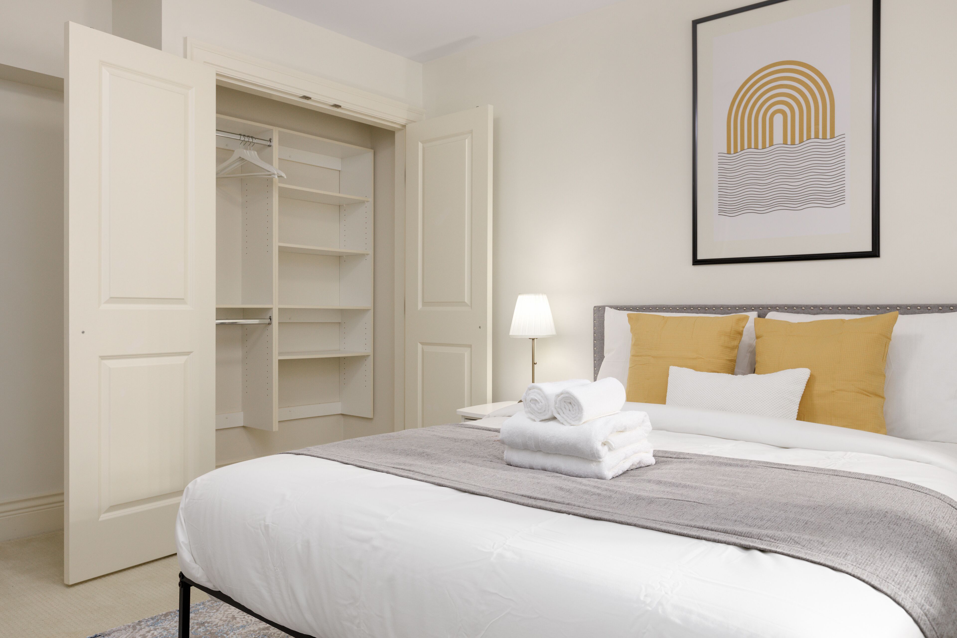 Quarto de hotel bem arrumado com uma cama, abajur, pilha de toalhas e armário com portas abertas.