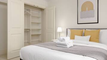 Quarto de hotel bem arrumado com uma cama, abajur, pilha de toalhas e armário com portas abertas.
