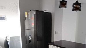 Cozinha com geladeira preta, bancada de granito e duas luminárias pendentes.