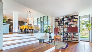 Uma sala de estar ampla com uma escada de madeira, uma área de jantar com toalha amarela e uma grande estante cheia de livros.