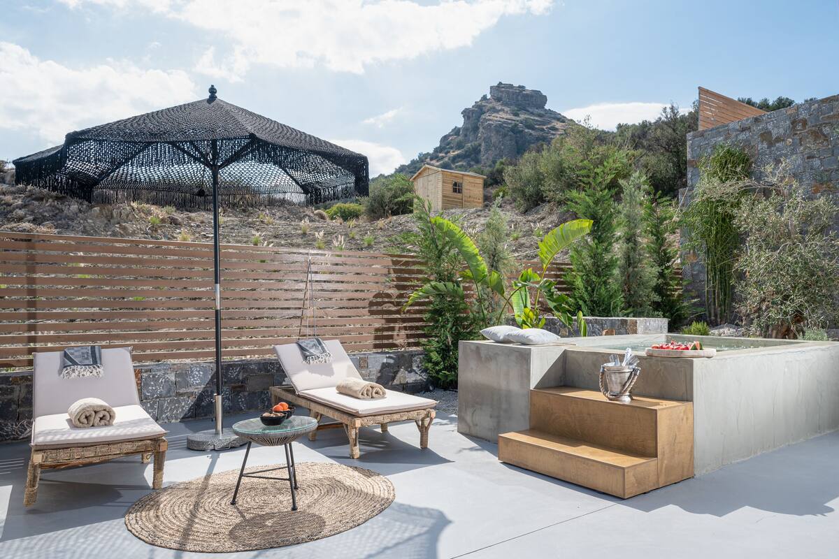 Um pátio externo com cadeiras de estar, uma mesa e um guarda-sol decorativo.