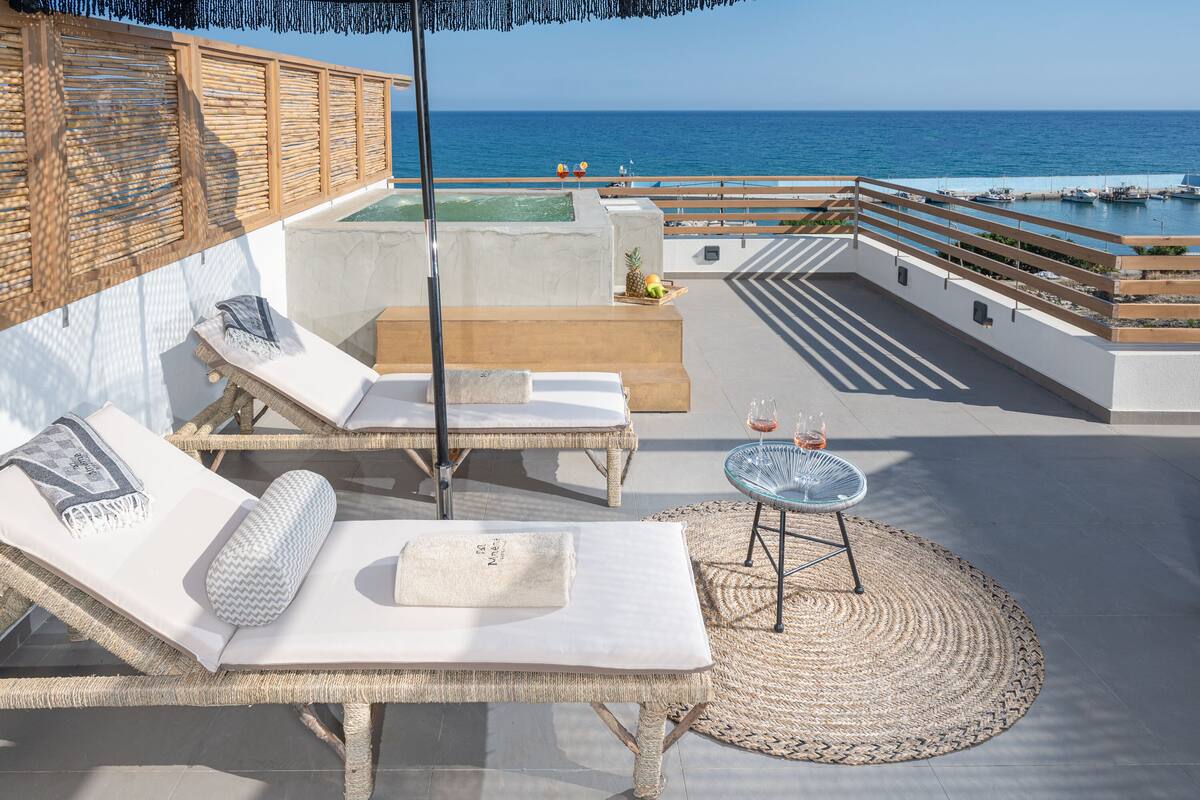 Terraço no telhado com cadeiras de descanso, uma mesa pequena com tampo de vidro e vista para o mar.