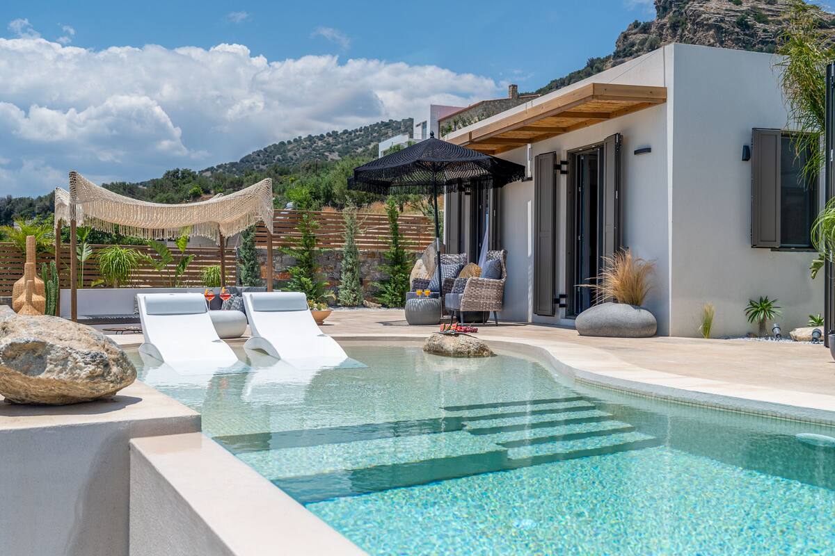 Uma área de piscina moderna com espreguiçadeiras, uma rede e vista para uma paisagem montanhosa.