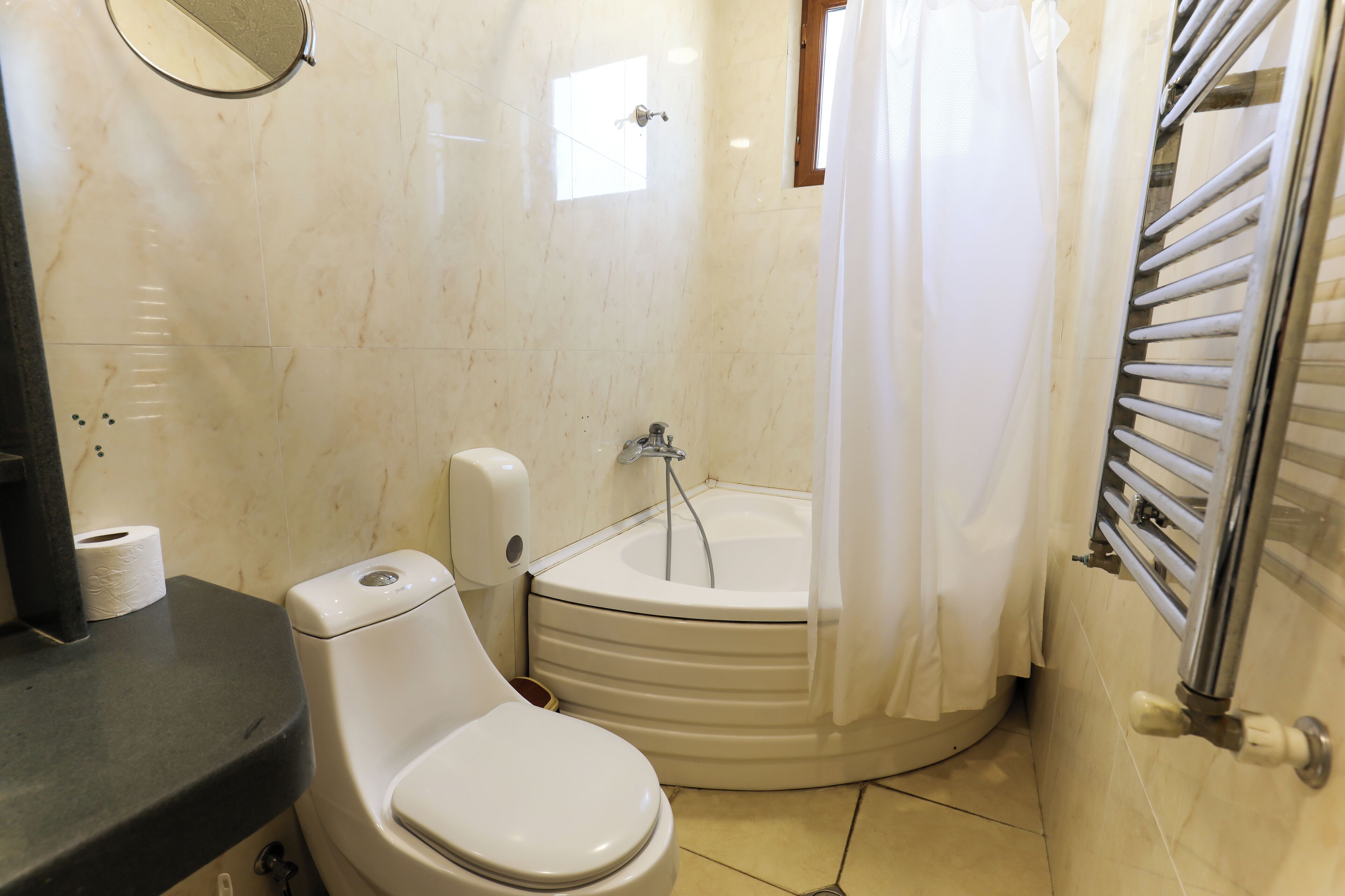 Um banheiro com vaso sanitário, pia, espelho, chuveiro e porta-toalhas.