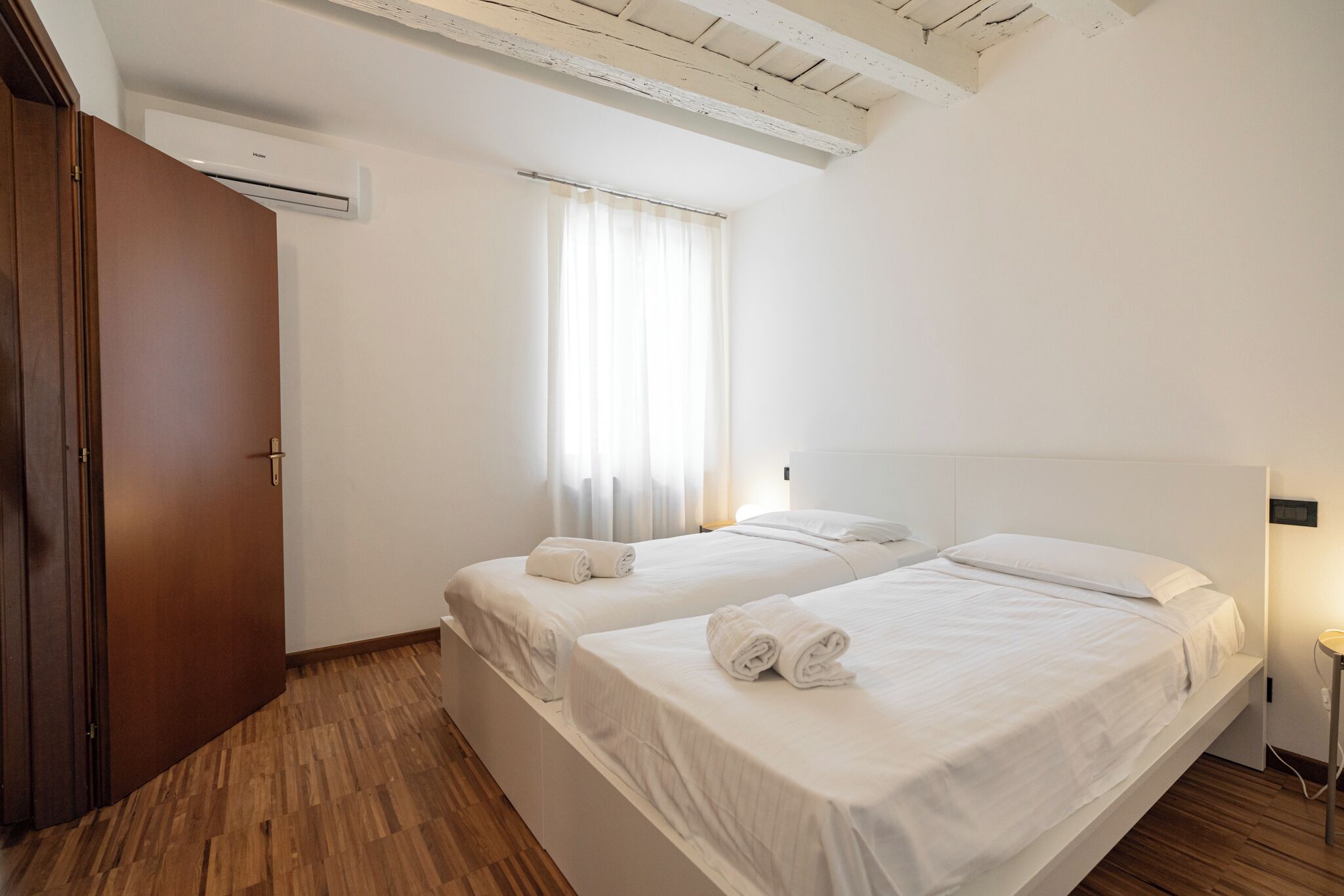 Quarto com duas camas, soalho de madeira, teto com vigas aparentes e um aparelho de ar condicionado.