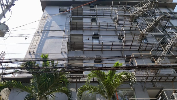 Um edifício de vários andares com escada de incêndio, palmeiras e uma placa com caracteres chineses.