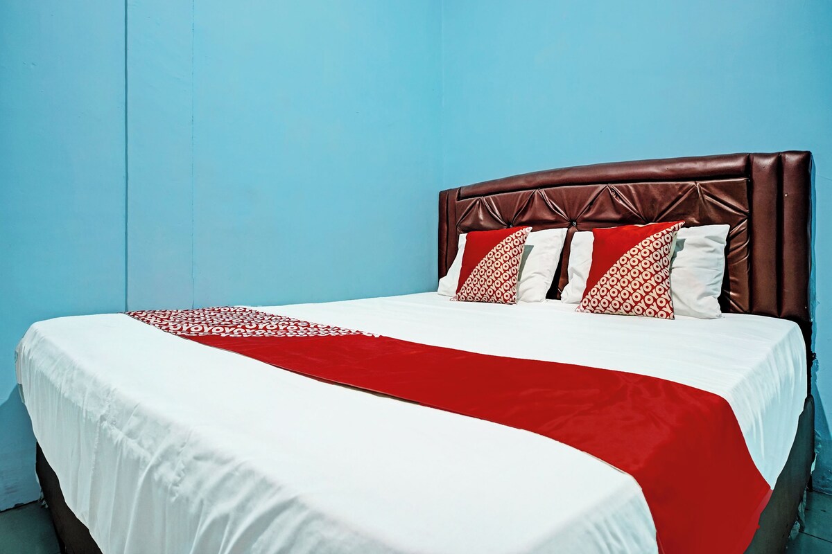 Uma cama bem arrumada com colcha branca e vermelha, cabeceira marrom e duas almofadas estampadas.