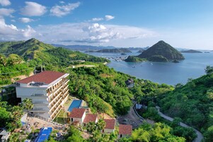Um hotel com vários andares, piscina, cercado por vegetação exuberante e com vista para uma baía com barcos.
