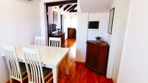 Uma sala de jantar com mesa de madeira e cadeiras brancas, um armário de madeira e uma porta que dá para outro cômodo.