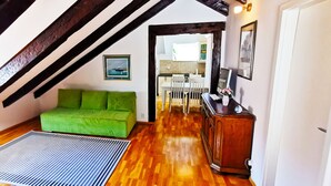 Um quarto com teto inclinado, um sofá verde, um armário de madeira e vista para uma cozinha.
