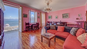 Uma sala de estar espaçosa com um sofá grande, um espaço de jantar e vista para o mar.