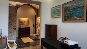 Um quarto com um arco de pedra, um aparador de madeira, uma cadeira branca, uma mesa preta e duas pinturas emolduradas na parede.