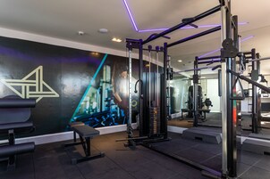 Uma academia com equipamentos de exercícios, um espelho grande e uma parede com padrão geométrico.