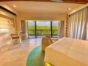 Quarto de hotel com uma cama grande, área de estar com cadeiras e vista para uma paisagem verde através de uma varanda.