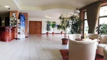 Um hall amplo com balcão de atendimento, área de estar e plantas em vasos.