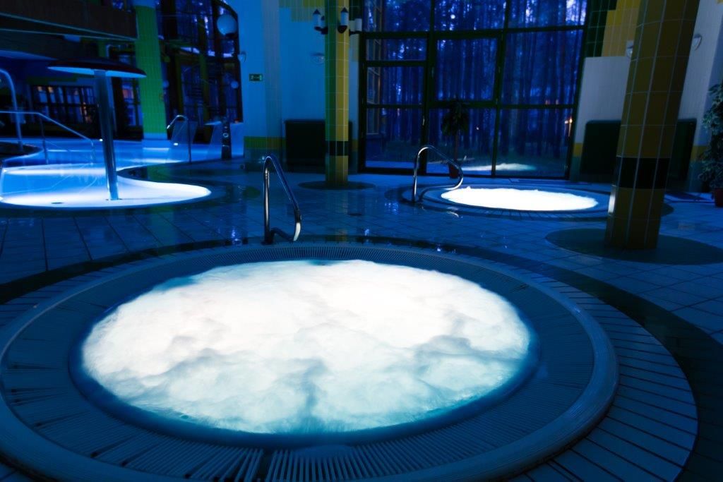 Área de piscina ao ar livre com hidromassagens e uma piscina central aquecida.