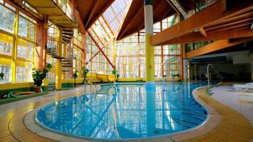 Piscina interna com revestimento de madeira, grandes janelas e uma escadaria central.