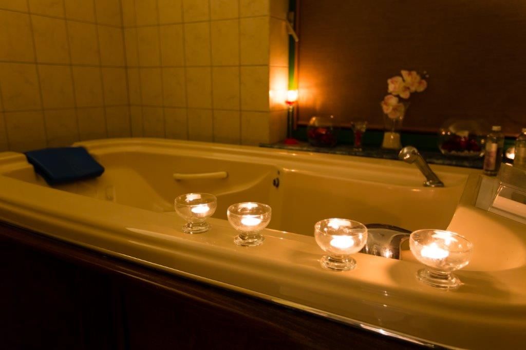 Casa de banho com banheira, lavatório e três velas acesas.