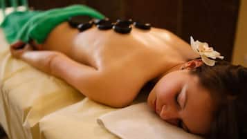 Uma pessoa recebendo uma massagem nas costas com pedras em uma mesa de massagem.