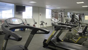 Uma academia com esteiras, aparelhos de musculação e uma televisão na parede.