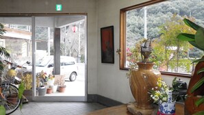 Uma área de recepção com uma grande janela, um vaso com flores e uma bicicleta estacionada do lado de fora.