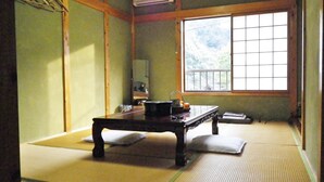 Um espaço com esteiras de tatame, uma mesa baixa, almofadas e uma janela com vista.