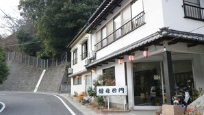 Um edifício japonês tradicional com uma placa, telhado de cerâmica e um muro de pedra ao fundo.