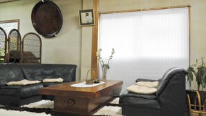 Uma sala de estar com um sofá de couro escuro, uma mesa de centro de madeira e uma janela grande com persianas.