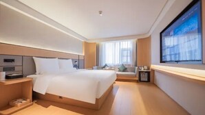 Quarto de hotel moderno com uma cama grande, televisão presa na parede, sofá e uma mesinha.