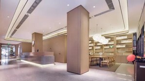 Um hall de hotel moderno com uma recepção, uma coluna central imponente e uma área de refeições com um lustre.