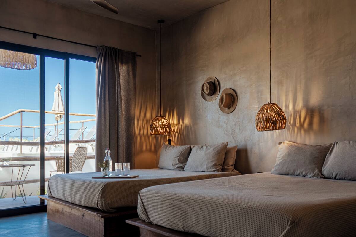 Quarto de hotel moderno com duas camas, uma janela grande com vista e uma varanda.