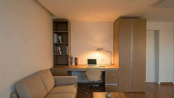 Uma sala de estar moderna com um sofá, uma escrivaninha com um laptop, uma estante de livros e uma mesa de centro.
