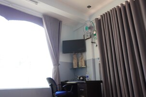 Quarto de hotel com escrivaninha, cadeira, televisão e cortinas.