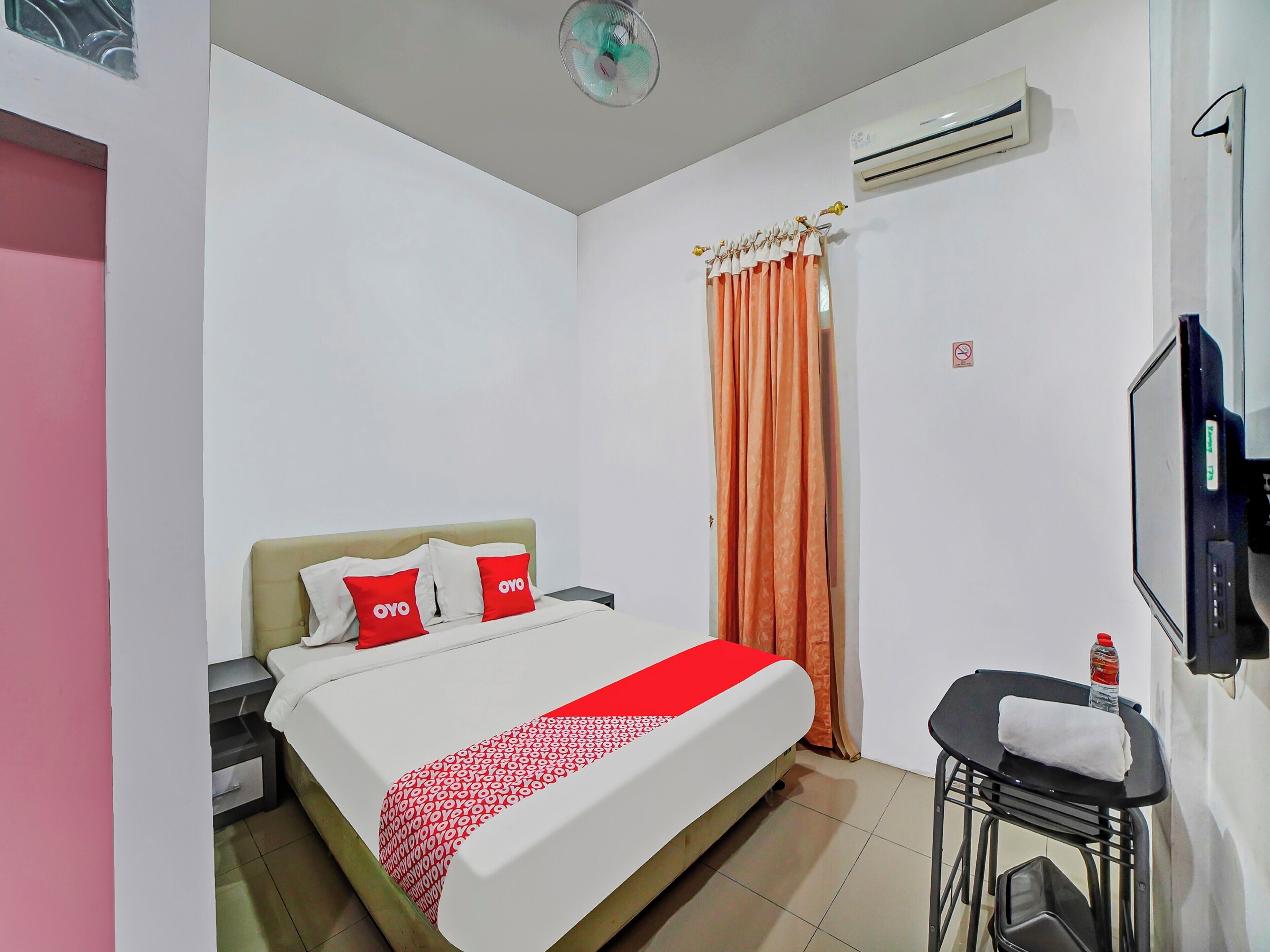 Quarto de hotel com cama, ar condicionado, televisão, cadeira e cortina.