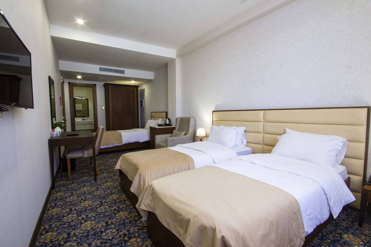 Quarto de hotel com duas camas, uma escrivaninha, uma cadeira e um espelho.
