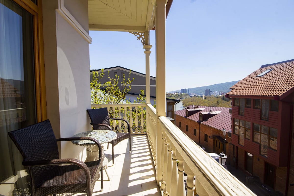 Uma varanda com cadeiras de vime e uma mesa, com vista para um horizonte urbano com edifícios e céu claro.