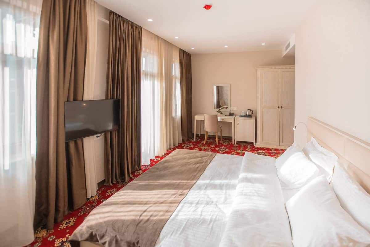 Quarto de hotel com uma cama grande, uma escrivaninha, uma cadeira, uma televisão e um guarda-roupa.