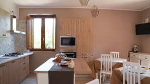 Cozinha moderna com armários de madeira, micro-ondas embutido e área de refeições com cadeiras brancas e uma mesa.