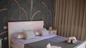 Cama bem arrumada com almofadas e toalha enrolada em estrutura branca.
