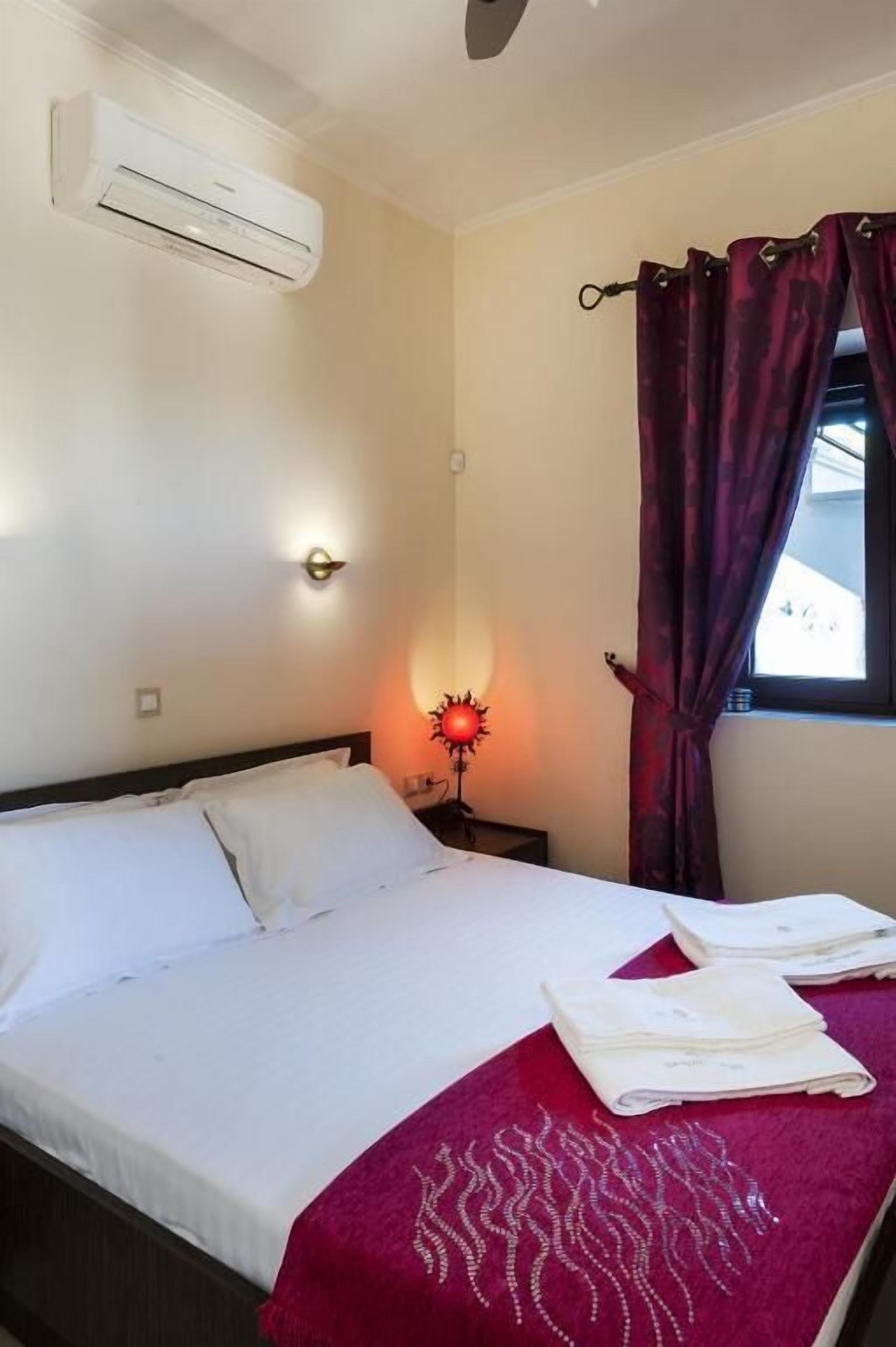 Quarto de hotel com cama, ar-condicionado, luminária na parede e janela com cortinas.