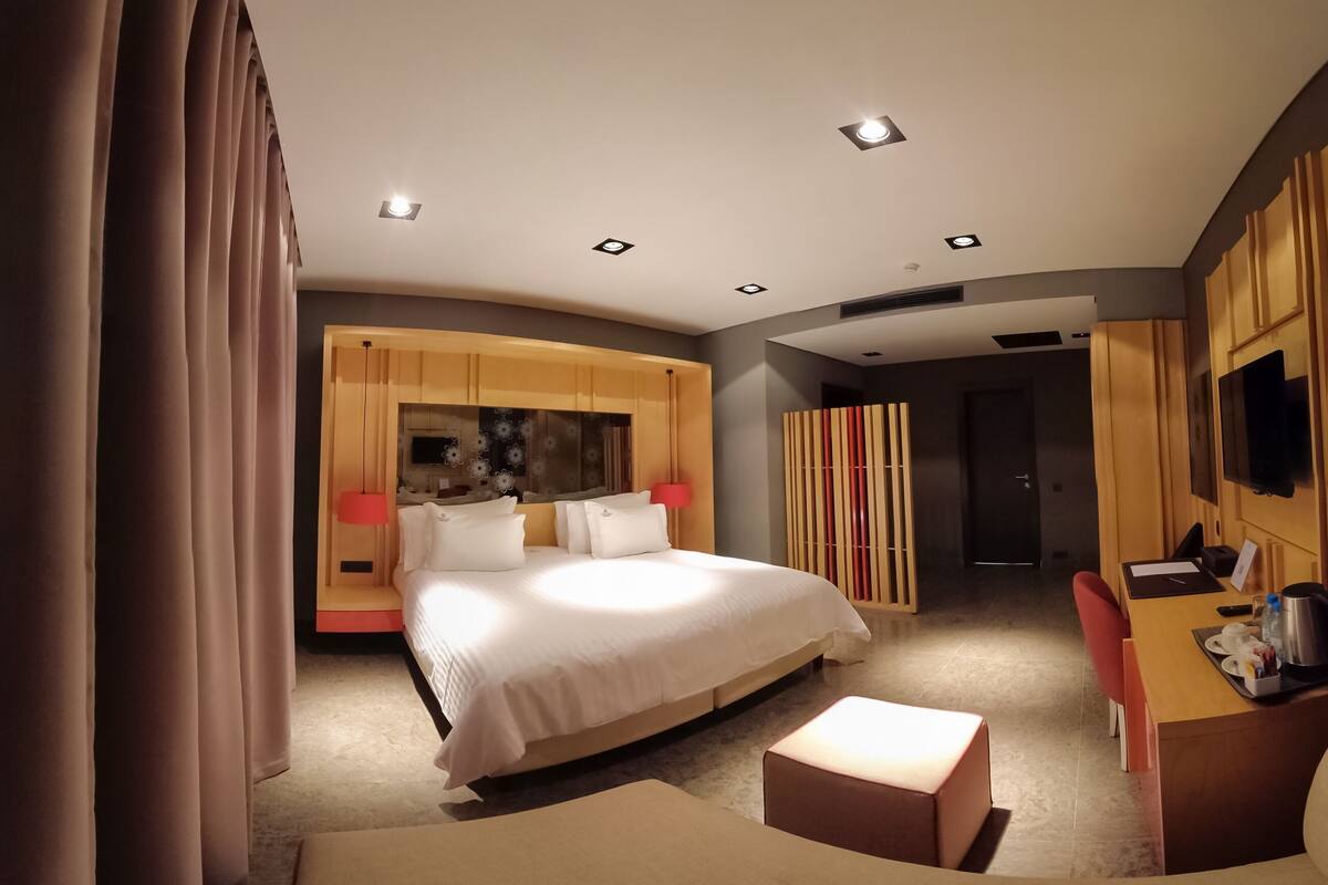 Quarto de hotel moderno com uma cama grande, uma escrivaninha, uma TV e um espaço de estar.