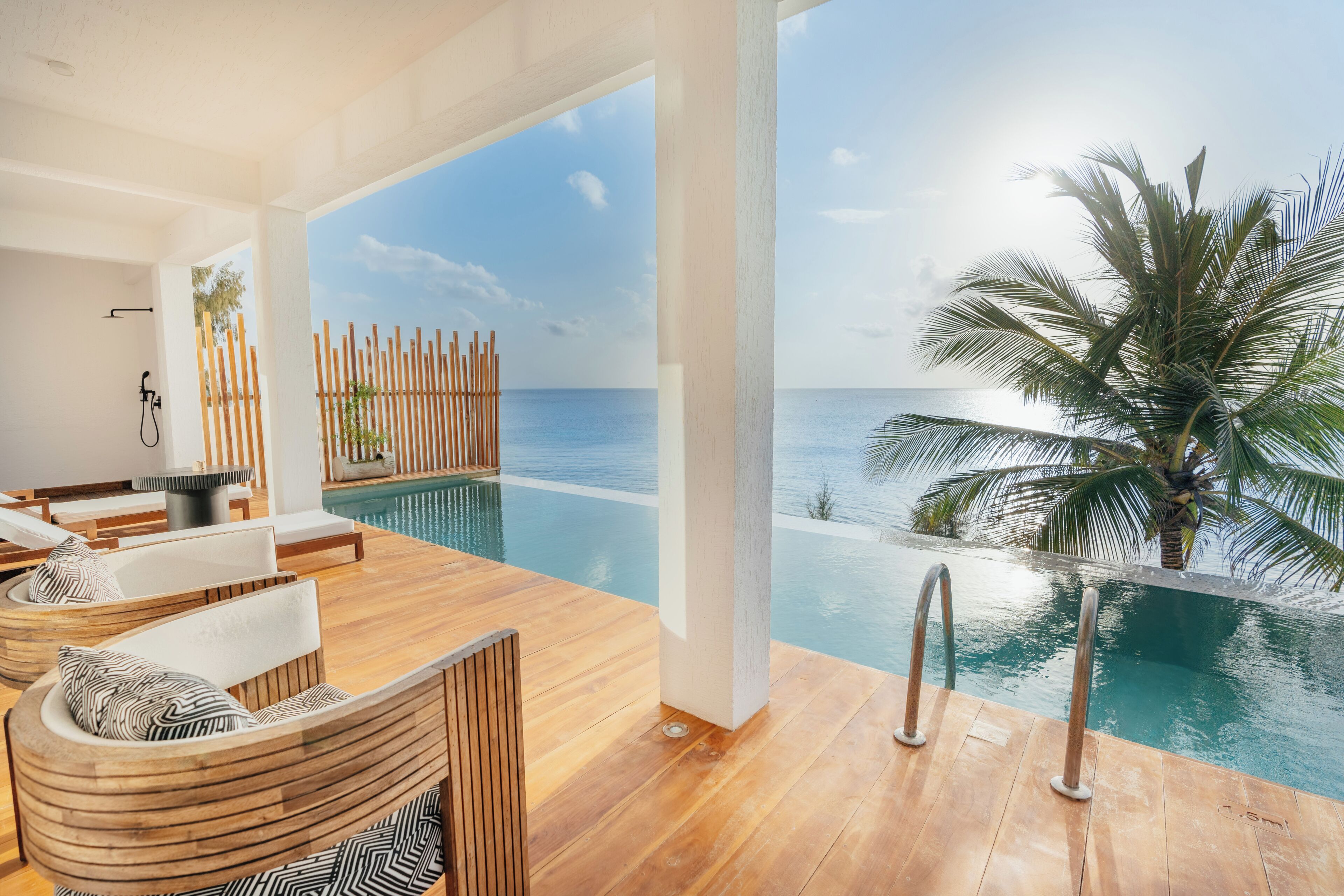Uma piscina infinita moderna com um deck de madeira, cadeiras de sol e vista para o oceano.