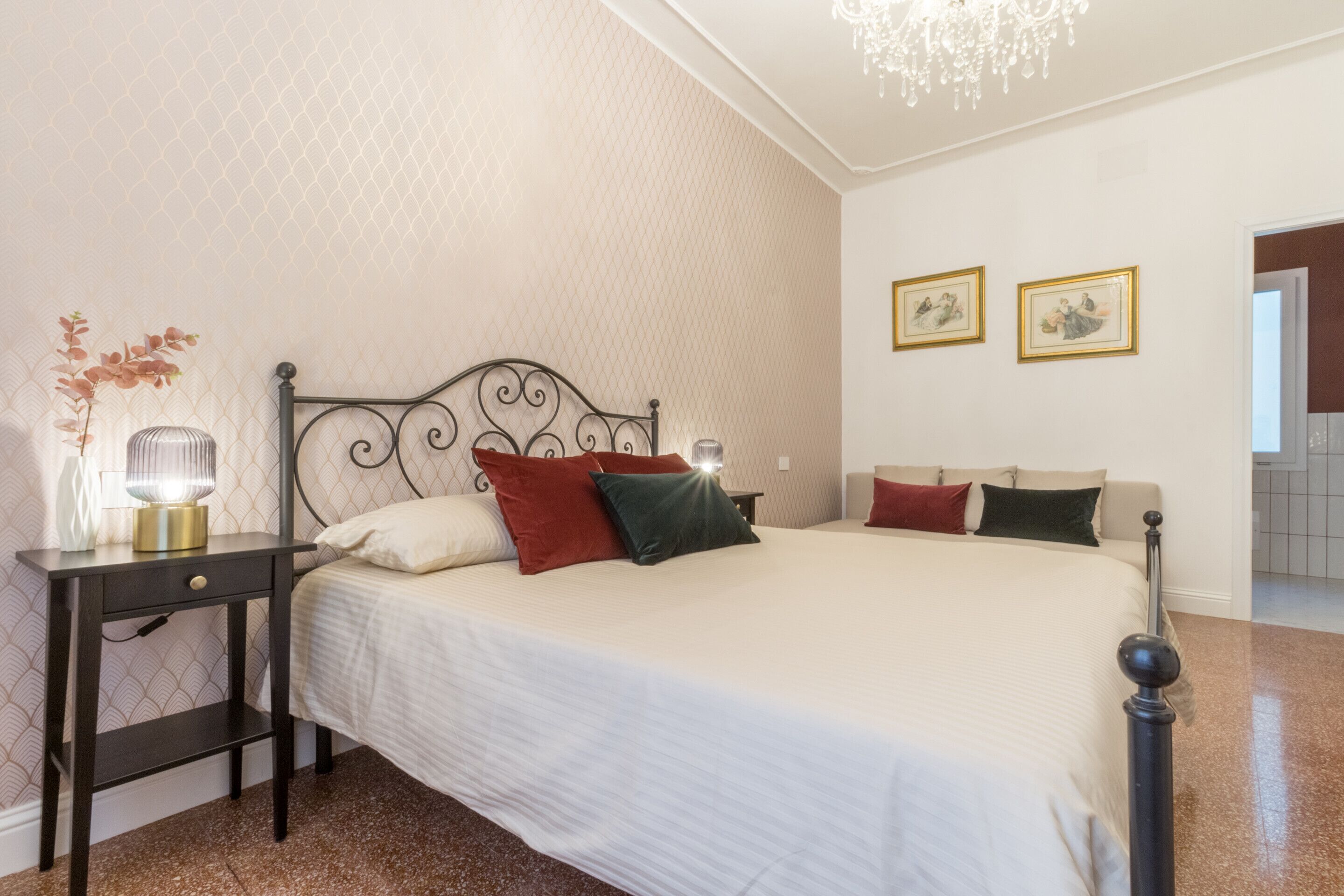 Quarto com cama, mesa de cabeceira, abajur e uma obra de arte na parede.