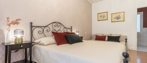 Quarto com cama, mesa de cabeceira, abajur e uma obra de arte na parede.